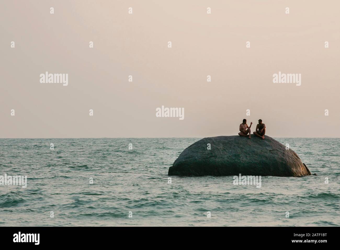 2 men sitting chatting on a sea rock Stock Photo - Alamy