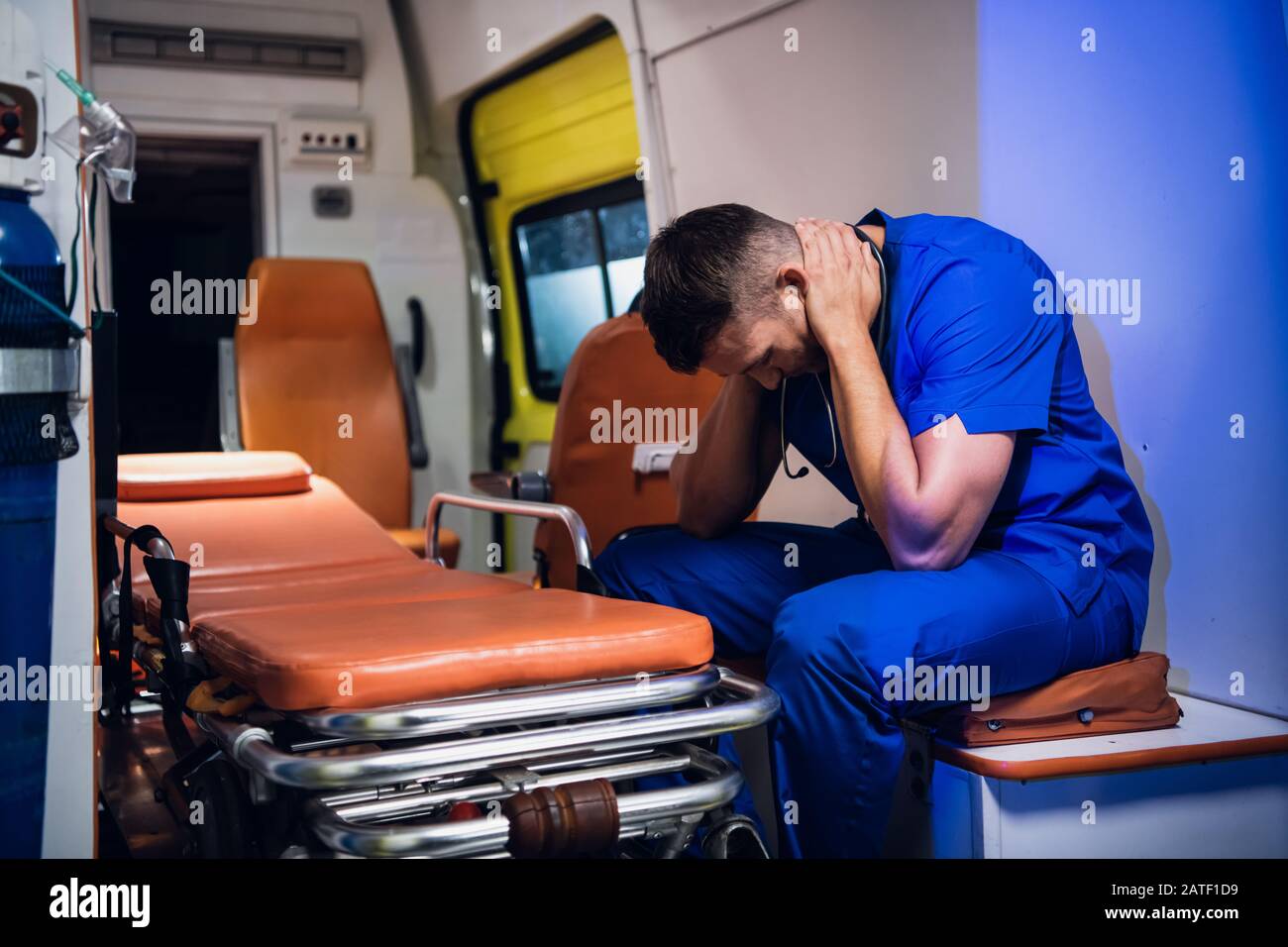 Tired corpsman sits inside the ambulance car and puts his hands on head ...