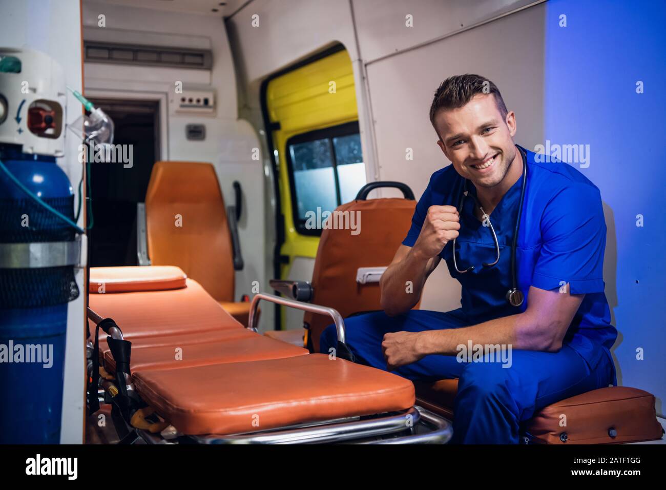 Young corpsman in medical uniform sits in the ambulance car and smiles ...