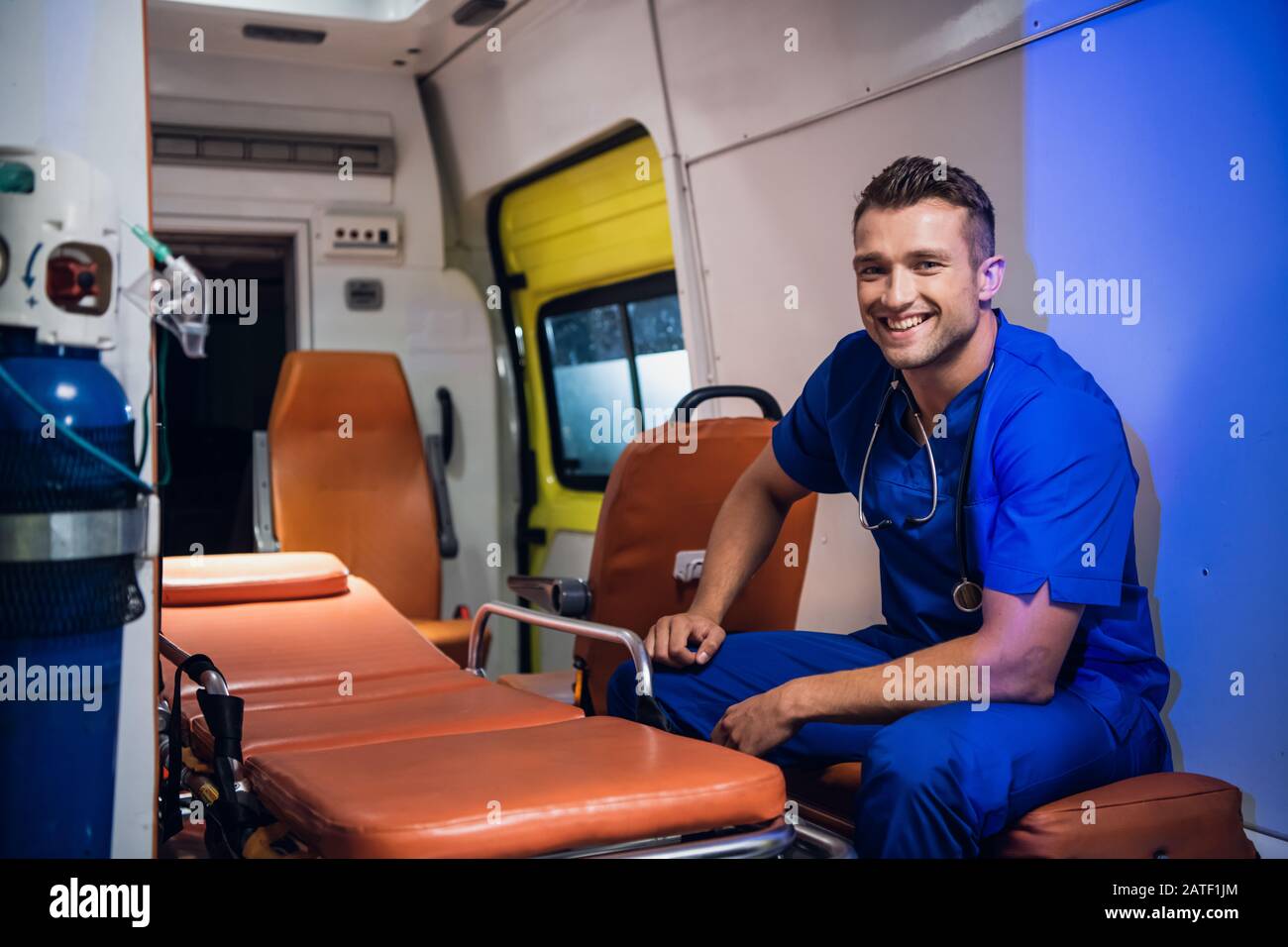 Young corpsman in medical uniform sits in the ambulance car and smiles ...