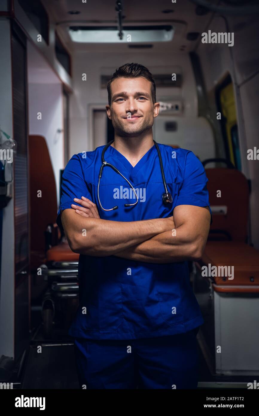 Smiling corpsman in blue medical uniform stands in the ambulance car at ...