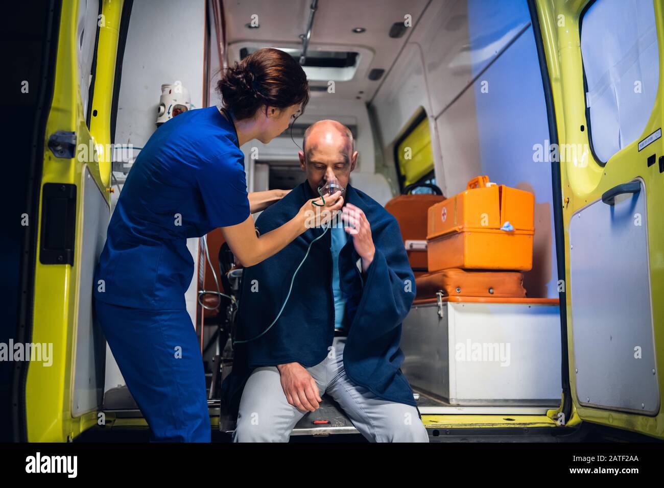 Young nurse in medical uniform puts oxygen mask on man sitting in ...