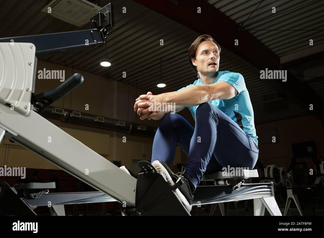 Caucasian male athlete sitting on modern indoor rower and resting after ...