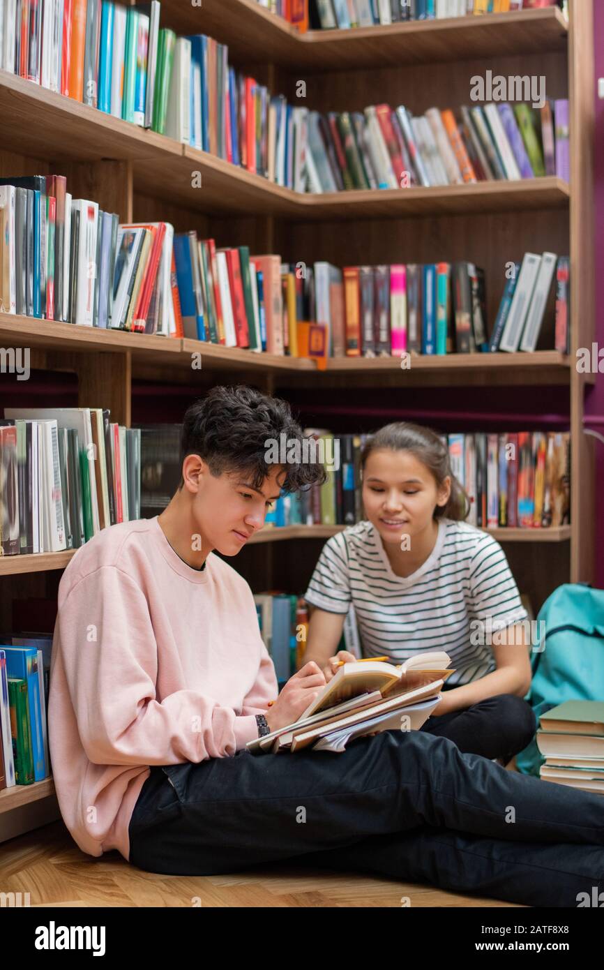 Two clever teenage students discussing passage from story in library ...