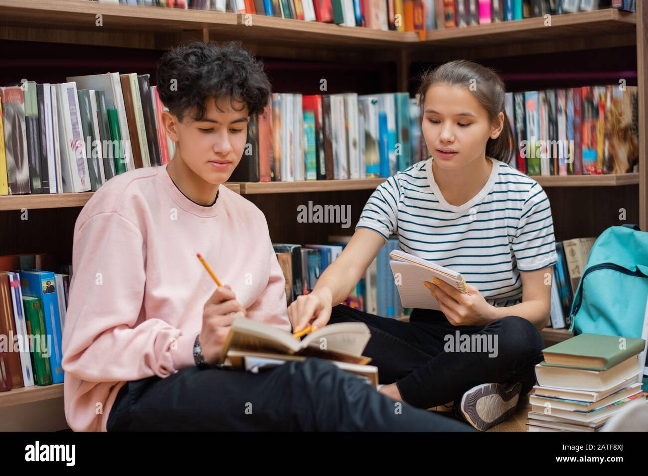 Clever confident girl pointing at page of book held by her classmate ...