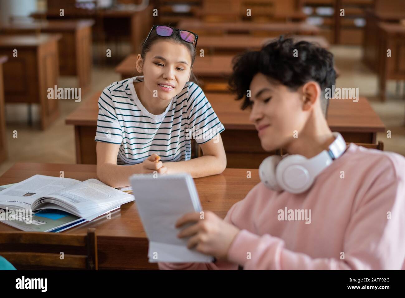 Clever teenage girl pointing at notes in notepad of classmate during ...