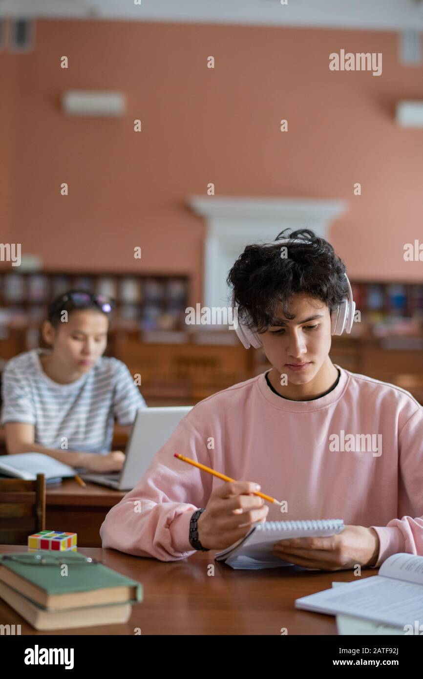 Serious college student in headphones listening to music while reading ...