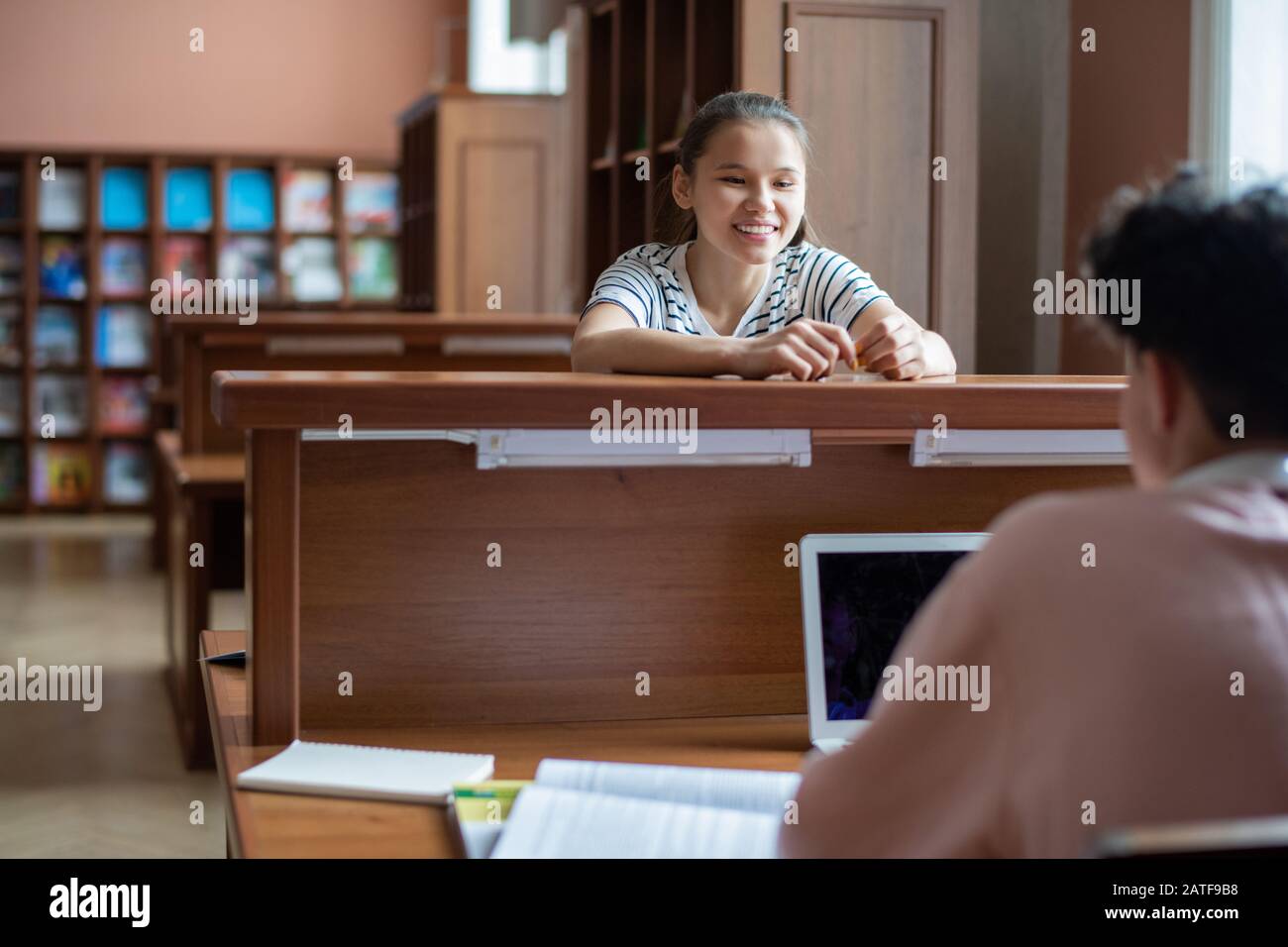 Happy teenage girl looking at her classmate with laptop during ...