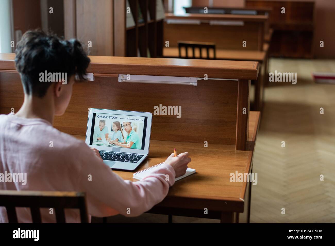Rear view of contemporary college student sitting by desk in front of ...