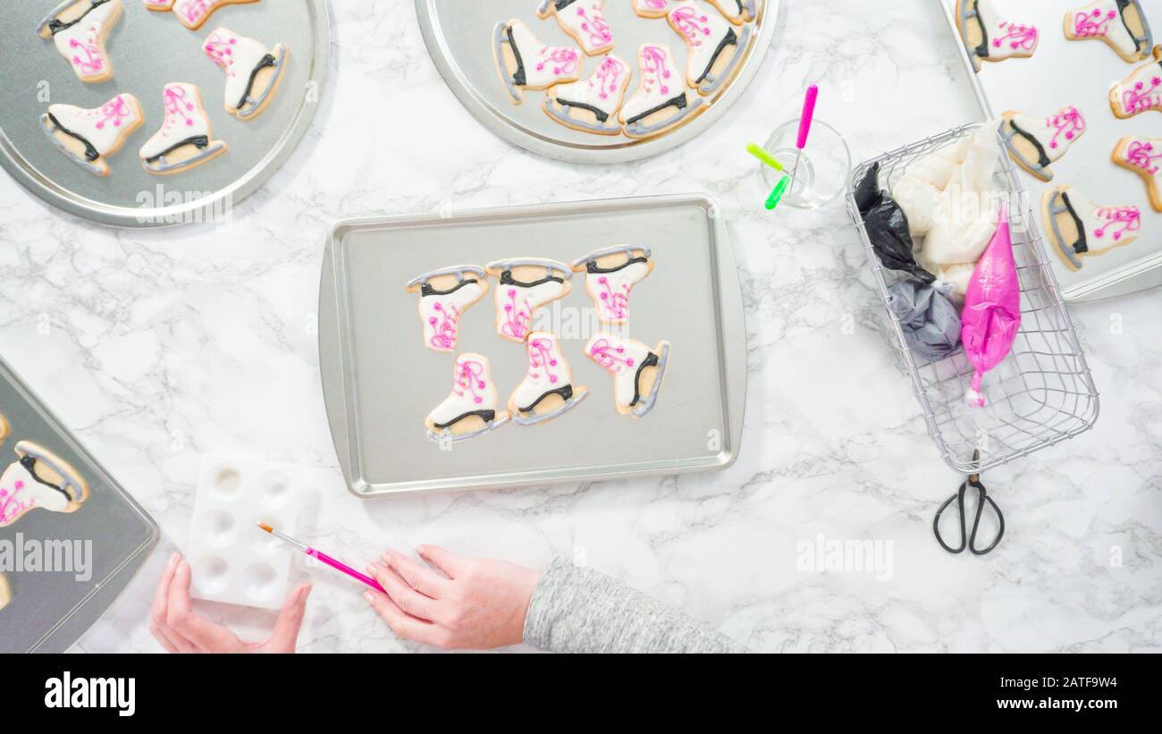Flat lay. Brushing edible glitter on iced figure skate sugar cookies ...