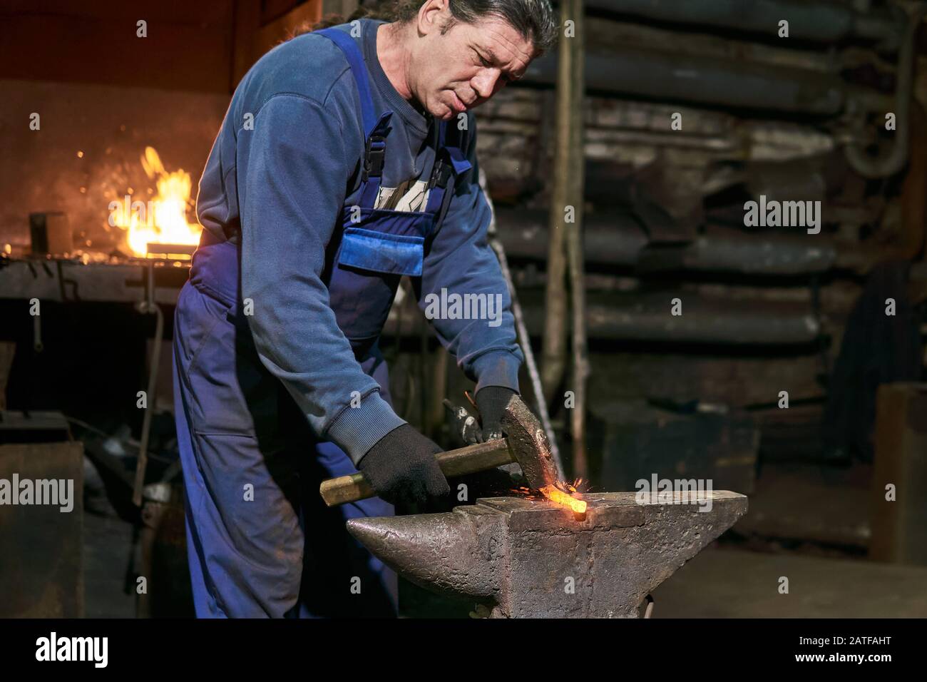 aged man blacksmith at work forges a red-hot piece of metal Stock Photo ...