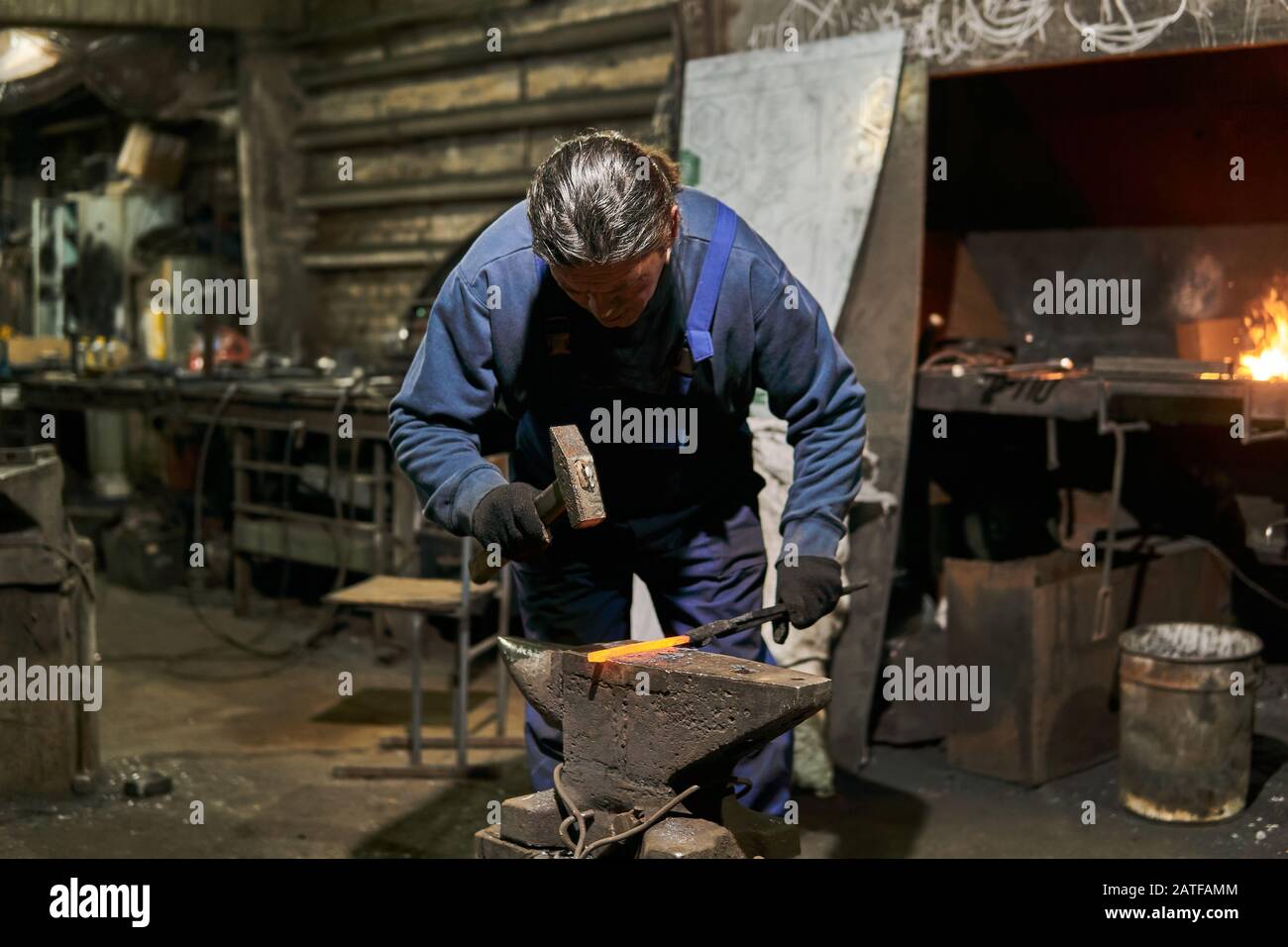 male traditional blacksmith at work forges a red-hot piece of metal ...