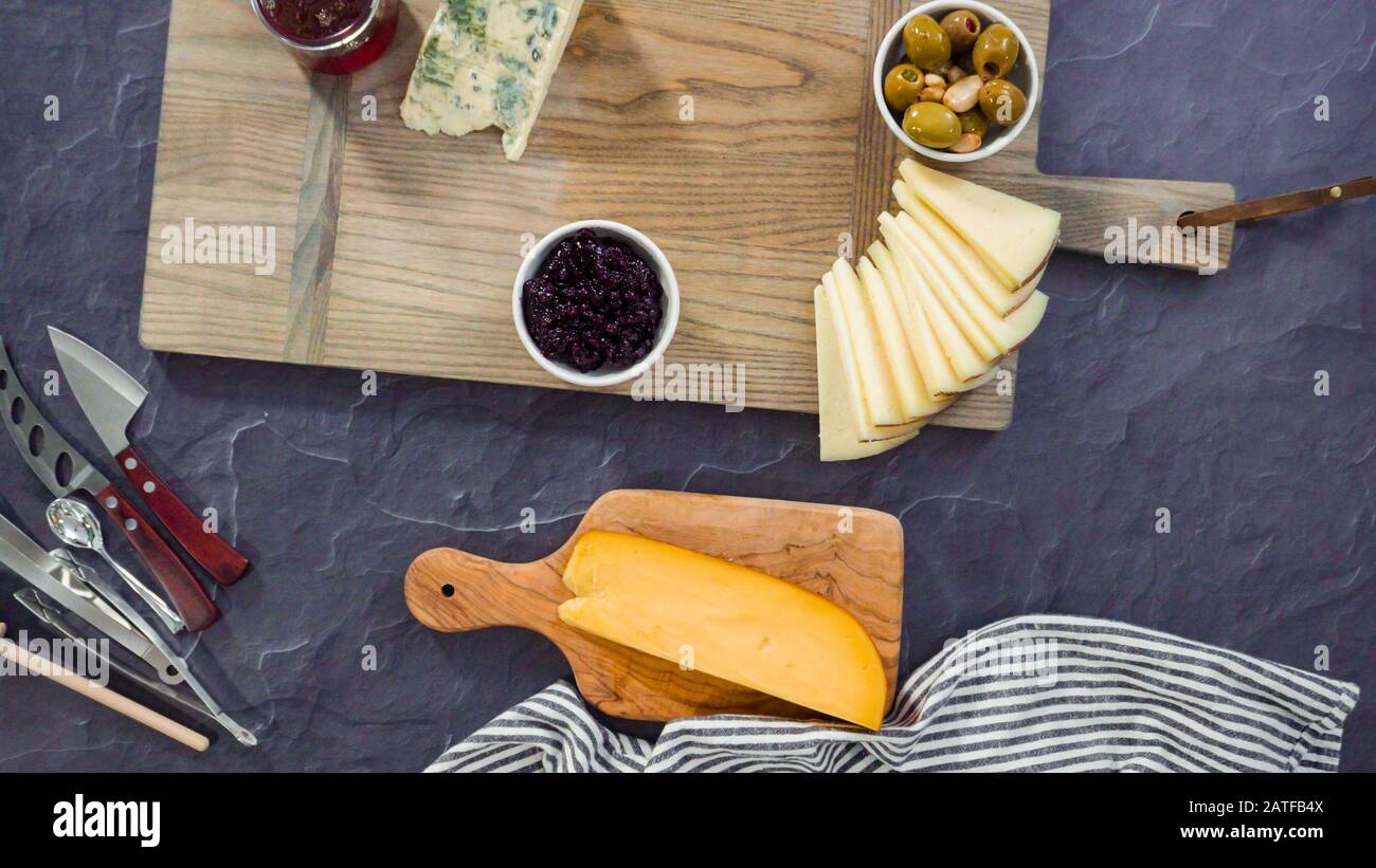 Flat lay. Arranging gourmet cheese, crakers, and fruits on a board for ...