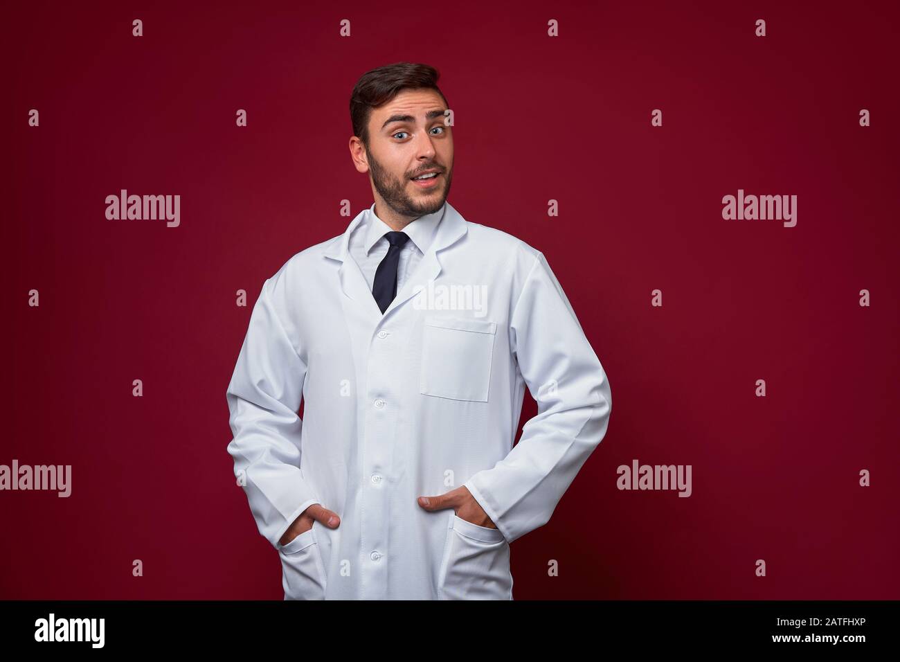 Young handsome modern doctor white medical gown stands in studio red ...
