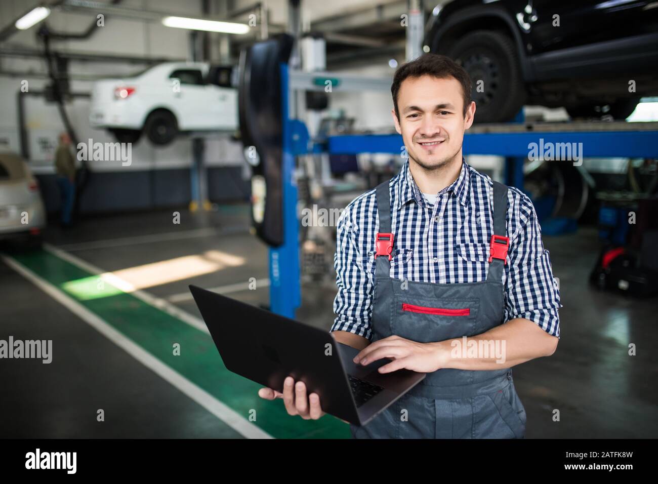 Smiling mechanic using a laptop computer to check a car engine Stock ...