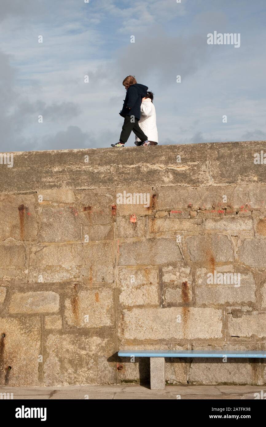 two people walking on a top of stone wall a dike in cold and cloudy ...