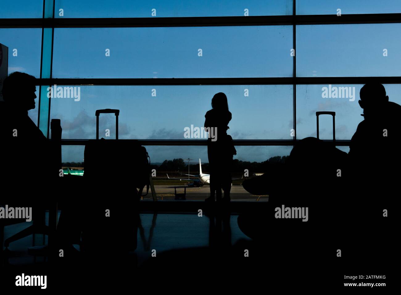 Silhouette of airline passengers in an airport lounge at the wide ...