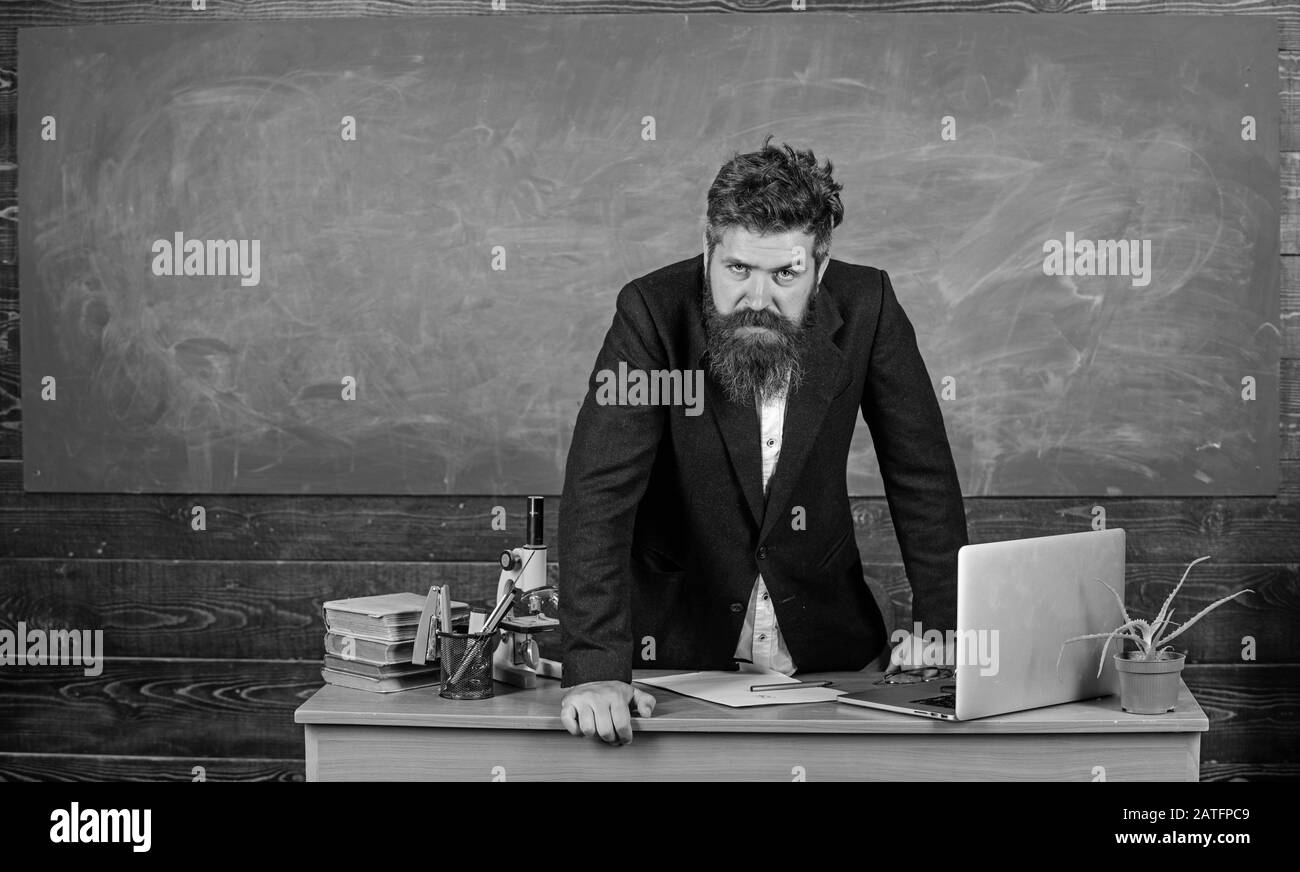 Teacher strict serious bearded man lean on table chalkboard background ...