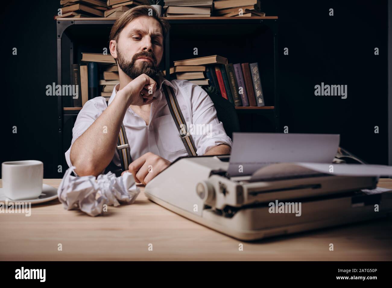 Thoughtful male writer sitting at his study desk by desktop typewriter ...