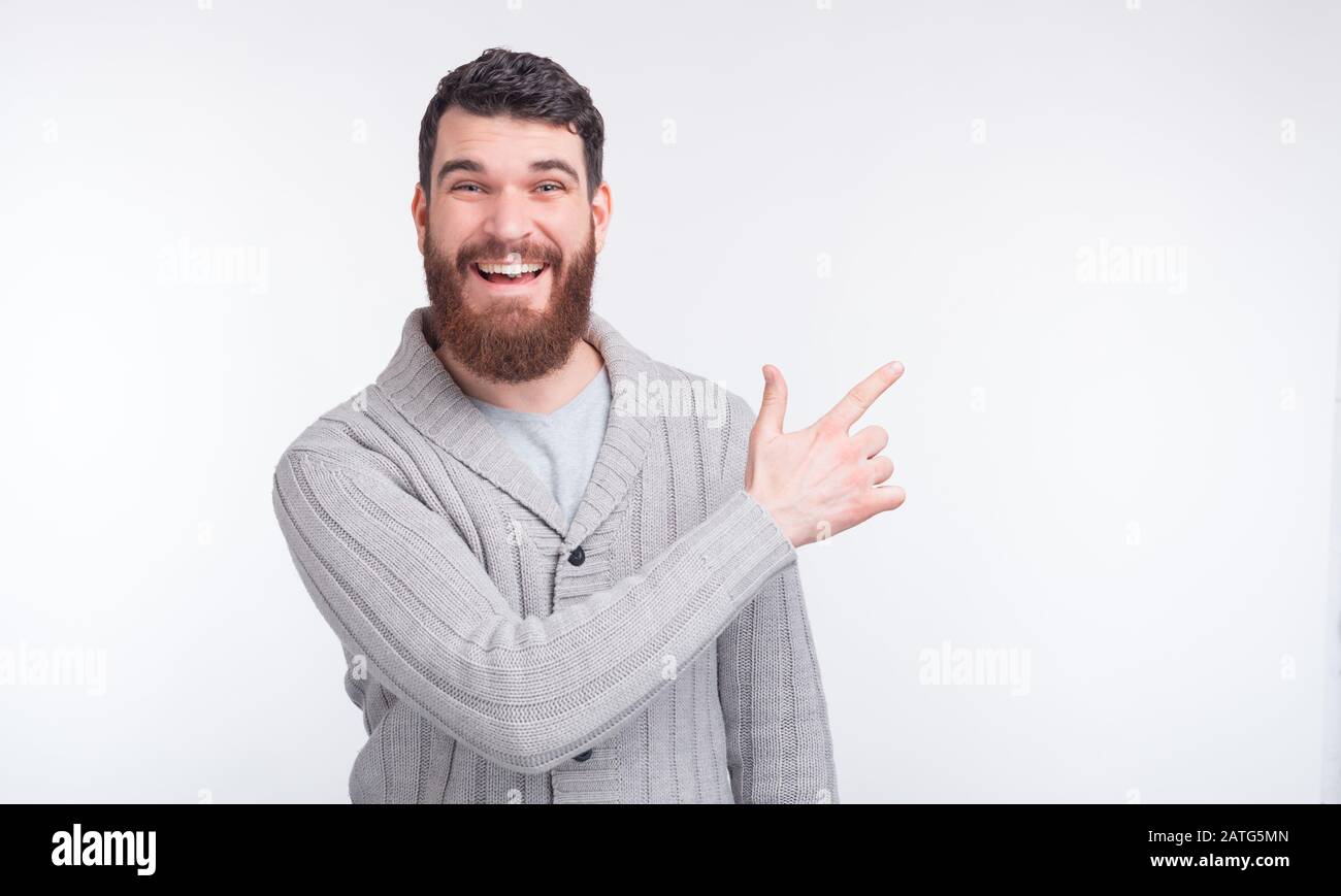 Happy young bearded man is pointing at his left on white background ...