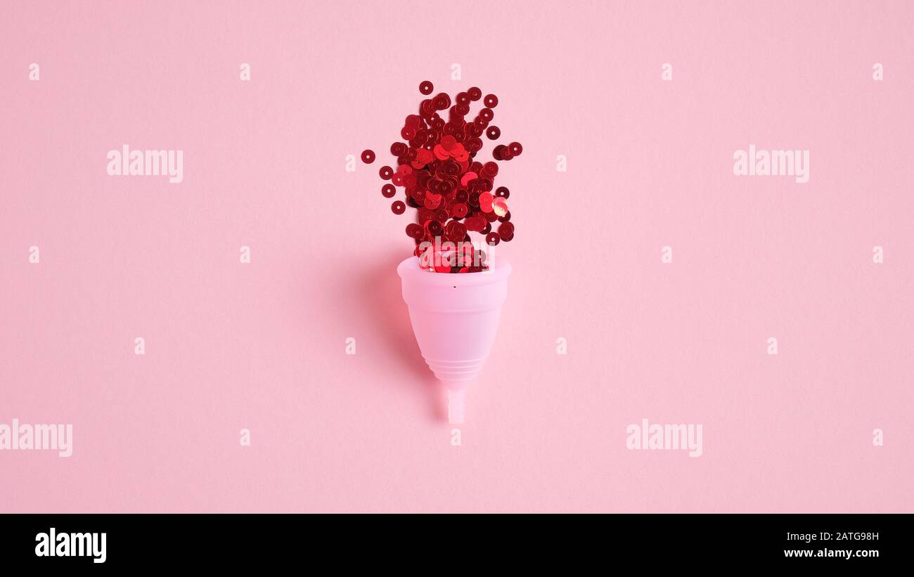 Reusable menstrual cup filled with red confetti on pink background ...