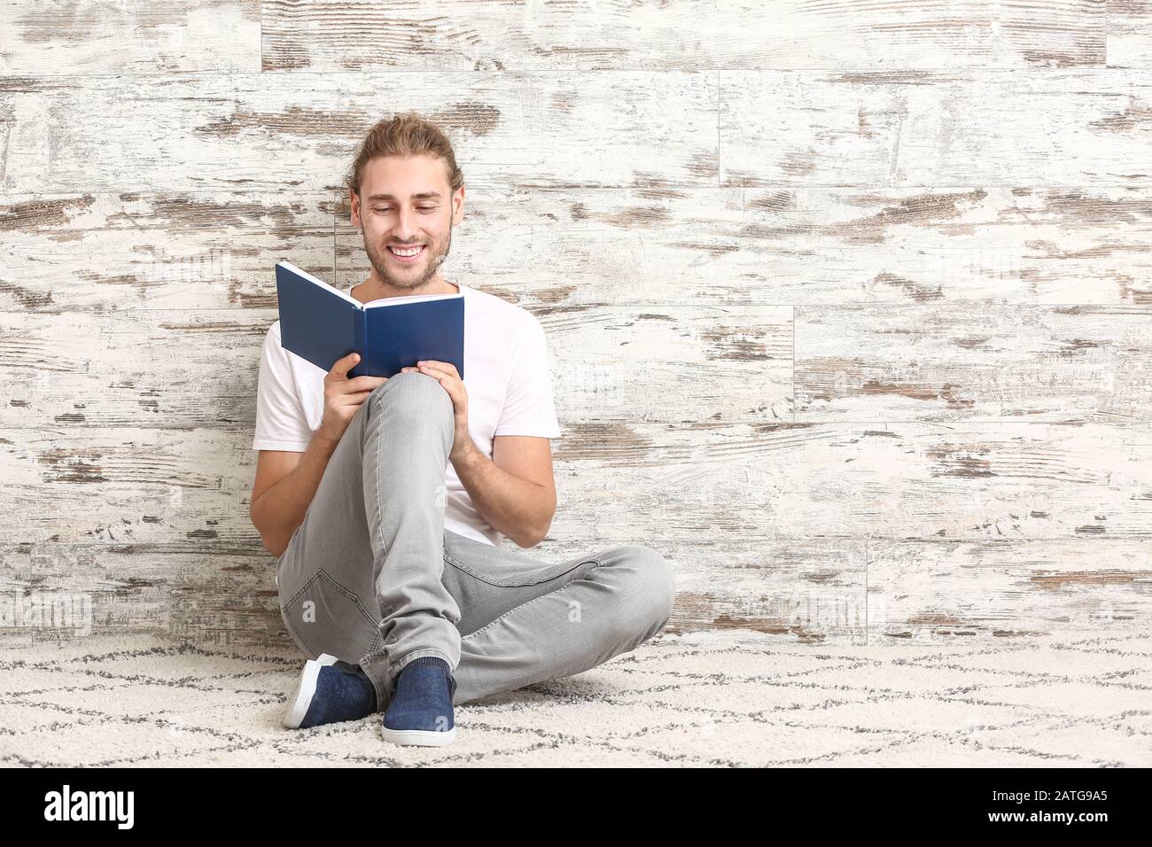Handsome man reading book near wooden wall Stock Photo - Alamy