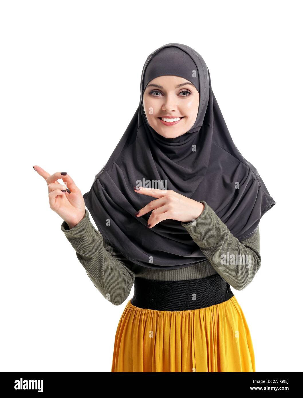Beautiful young Muslim woman pointing at something on white background ...