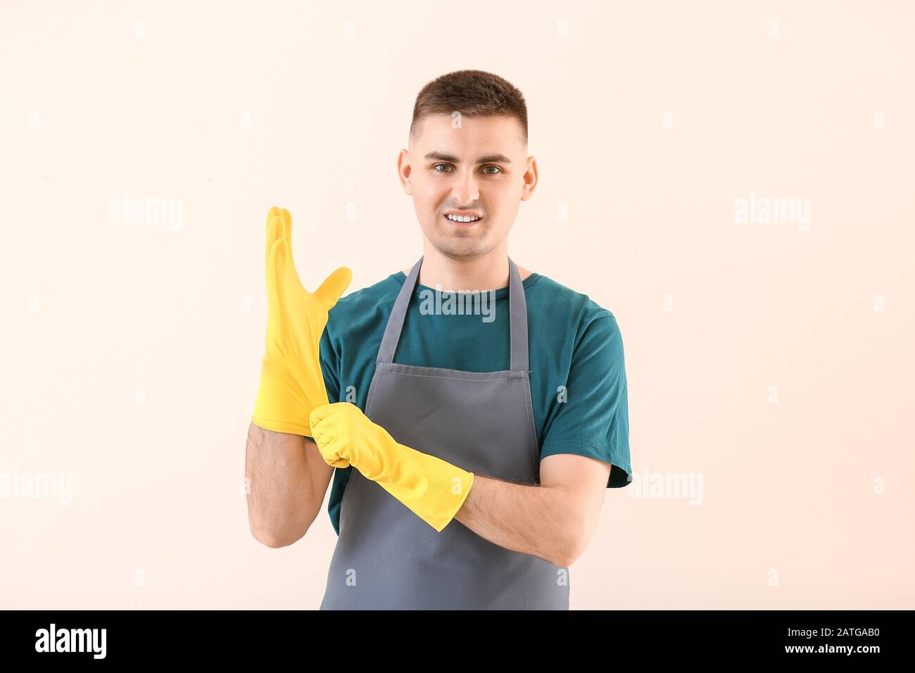 Portrait of janitor putting on rubber gloves against light background ...