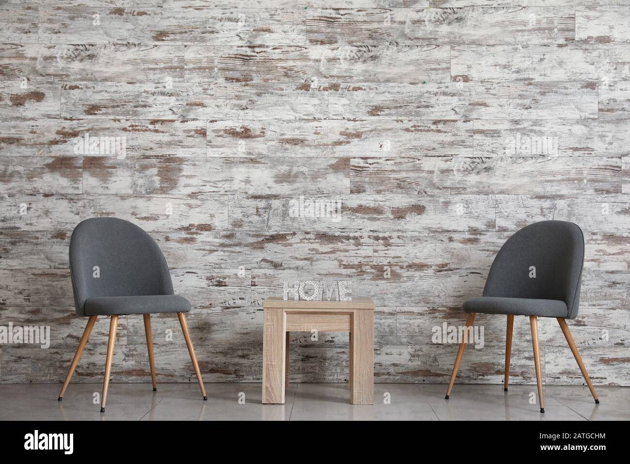 Stylish chairs with table near wooden wall in room Stock Photo - Alamy