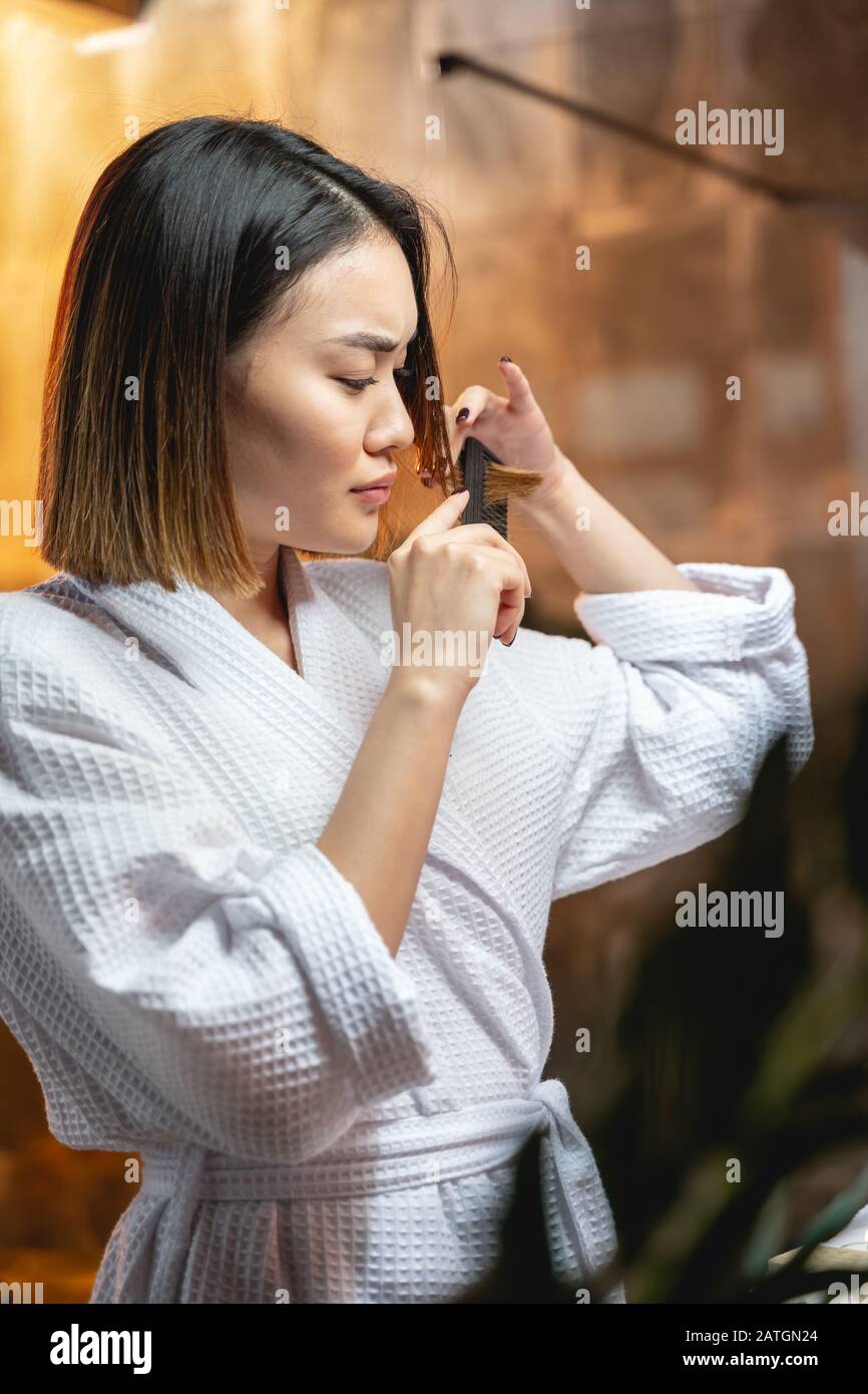 Sad Asian lady in white bathrobe brushing her hair Stock Photo - Alamy