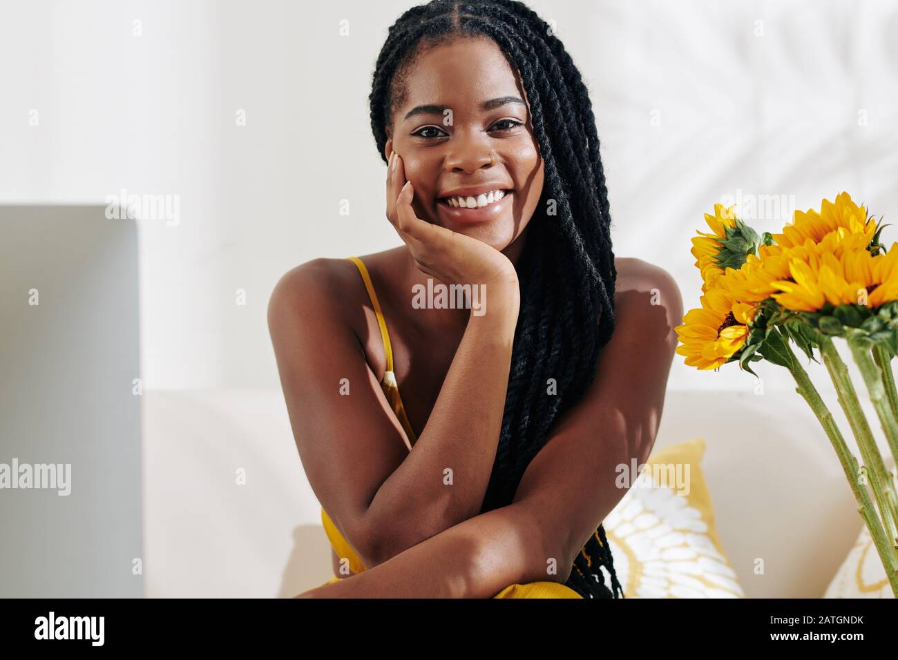 Lovely charming young Black woman sitting on sofa at home and smiling ...