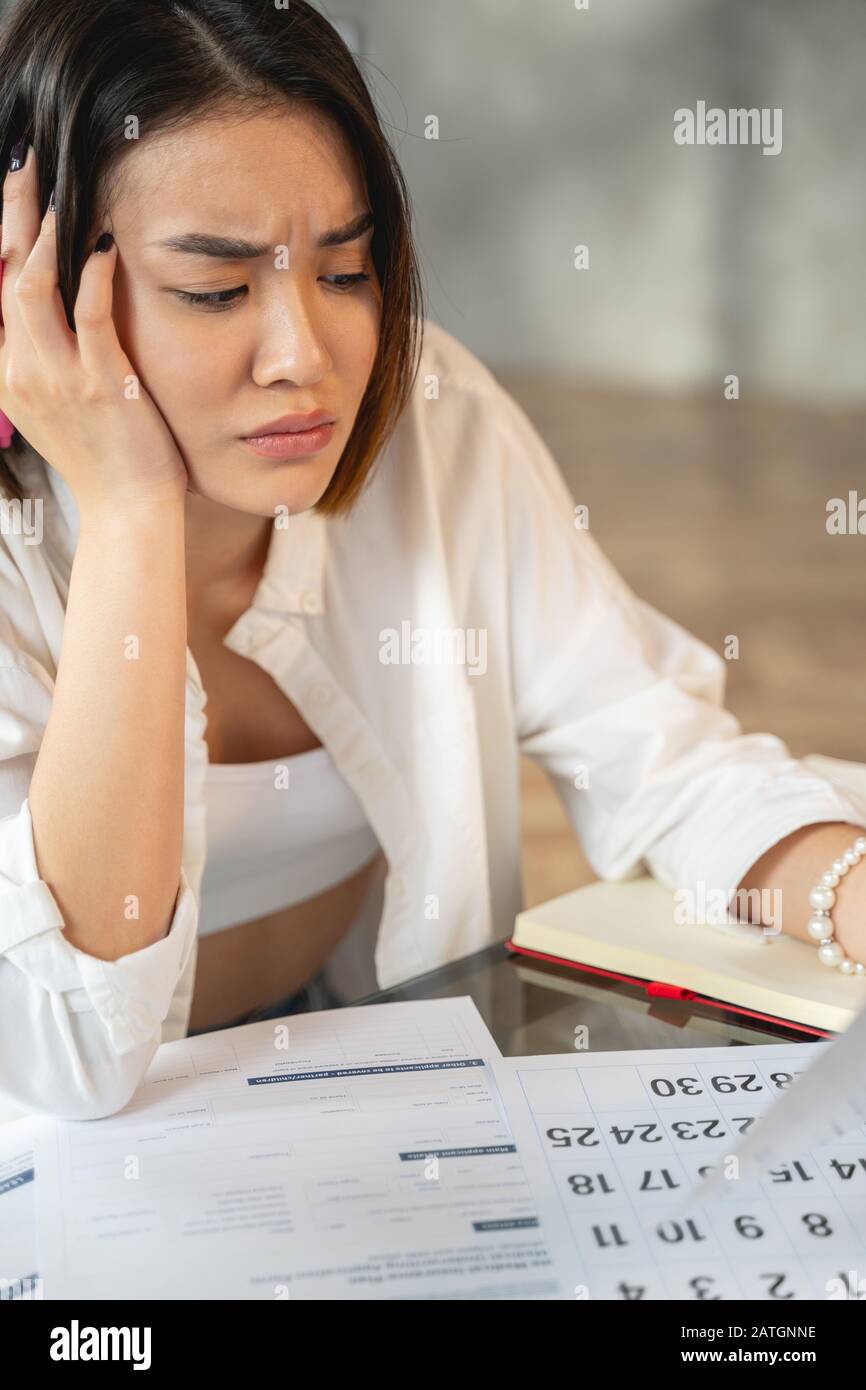 Asian frowning woman working with papers and laptop Stock Photo - Alamy