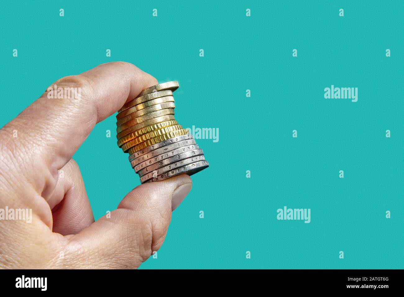 A persons left hand holds a stack of Euro coins between their fingers ...