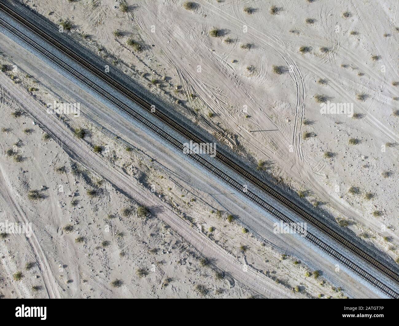 Train tracks run diagonally through the desert. Two sets of tracks side ...