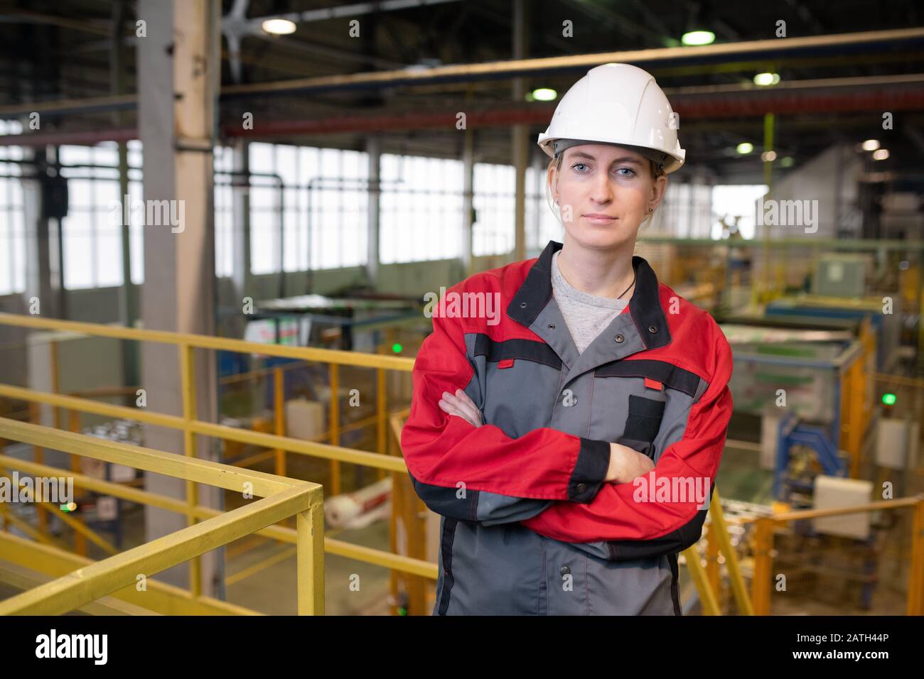 Portrait of serious confident female factory worker in hardhat crossing ...