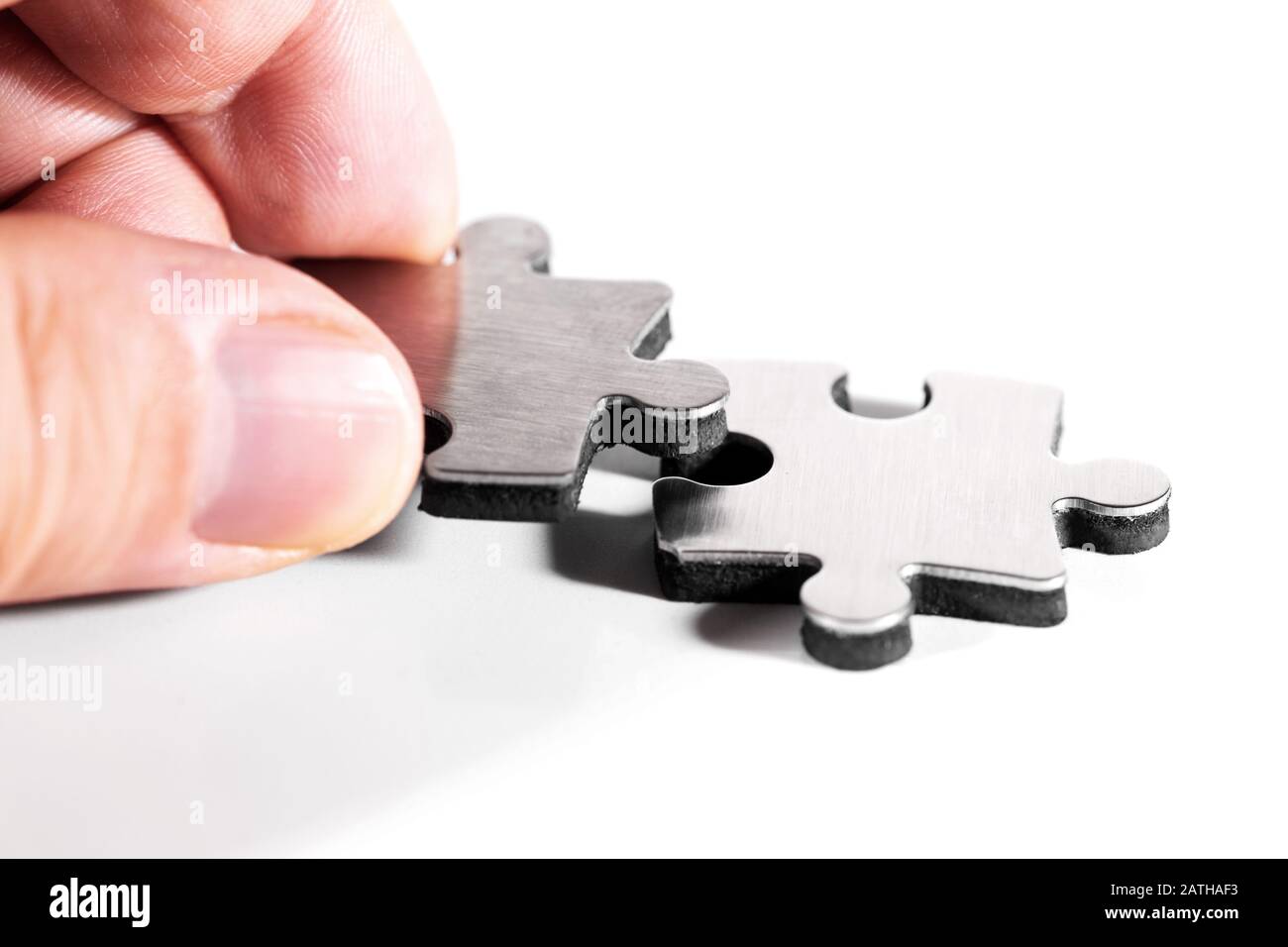 Two puzzle pieces are put together, closeup with male hand, isolated ...