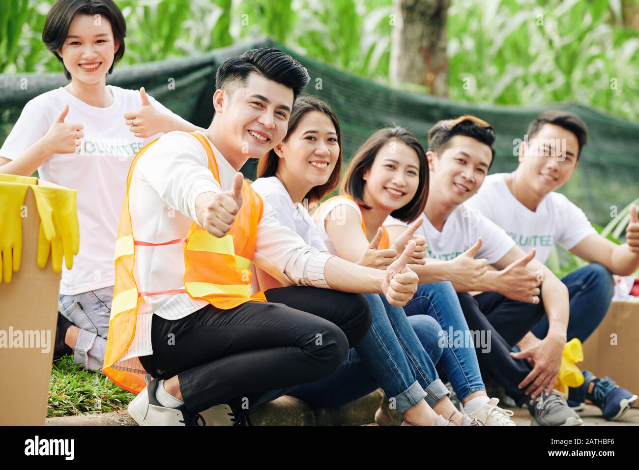 Happy young Asian students volunteers sitting outdoors, smiling and ...