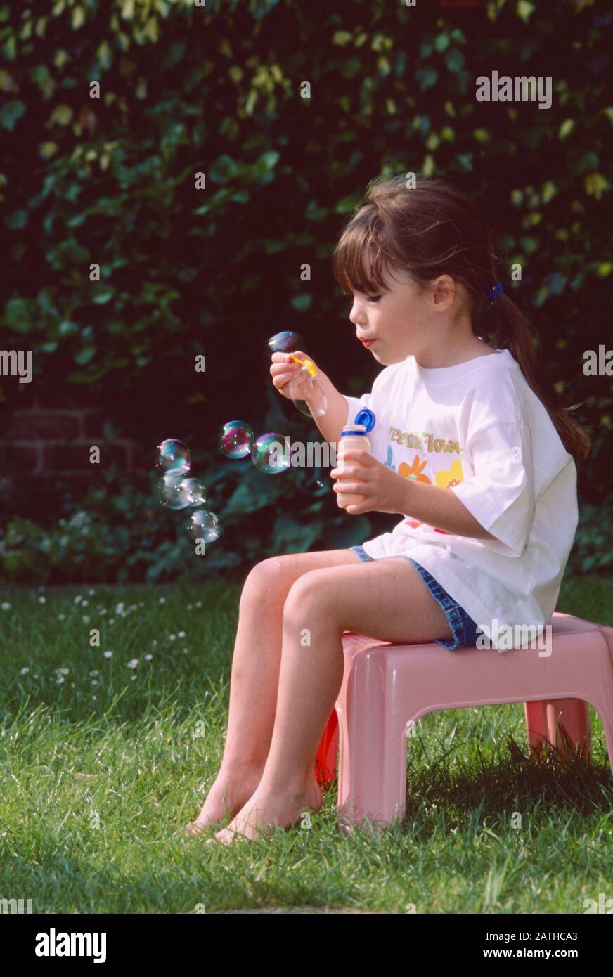 young girl outside in garden blowing bubbles holding pot of bubble ...
