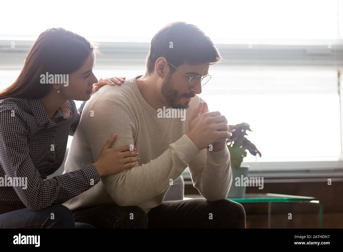 Couple sit on sofa caring wife hugs disappointed sad frustrated husband ...