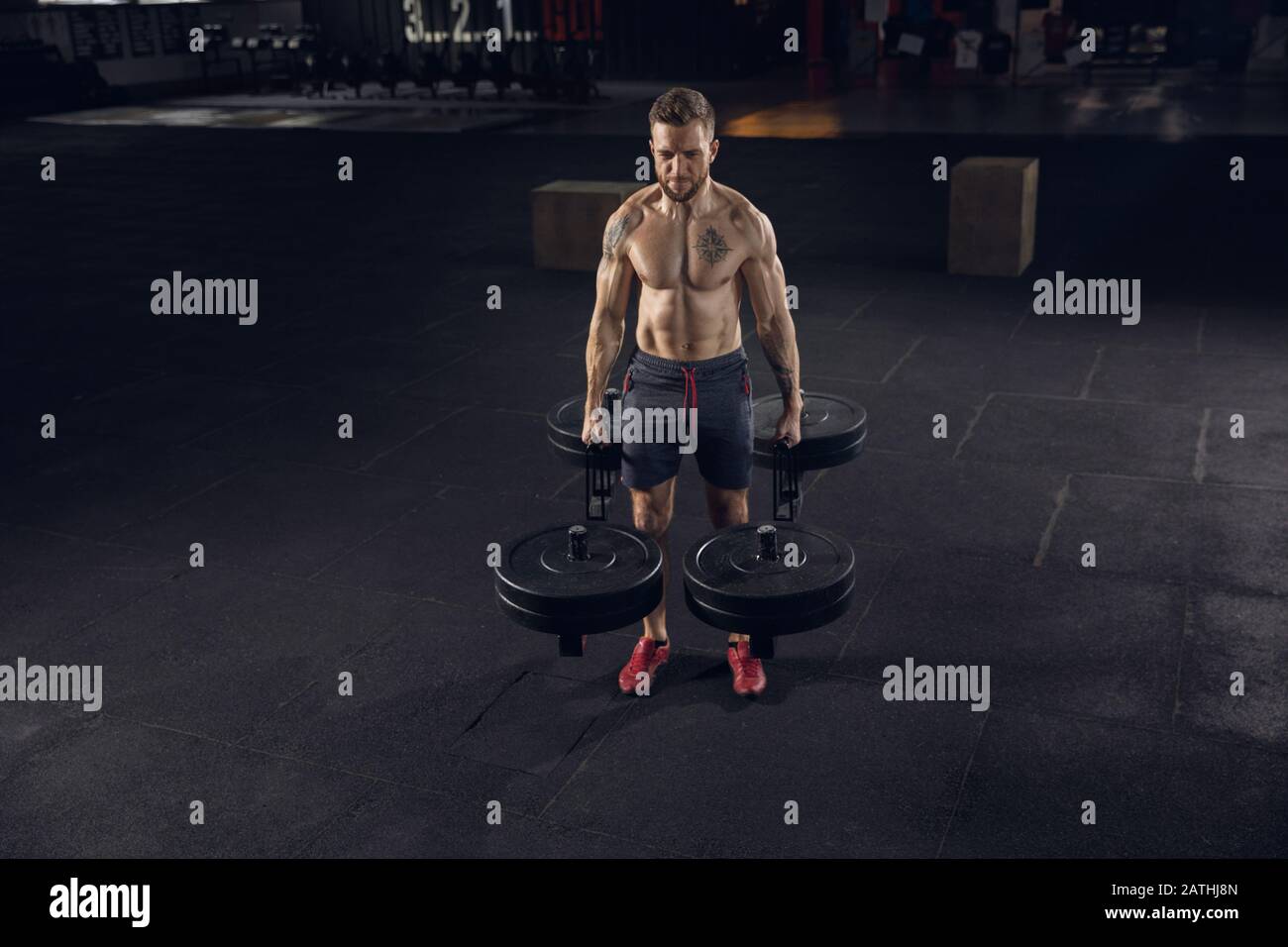 Young healthy man, athlete doing exercises, posing with barbell in gym ...