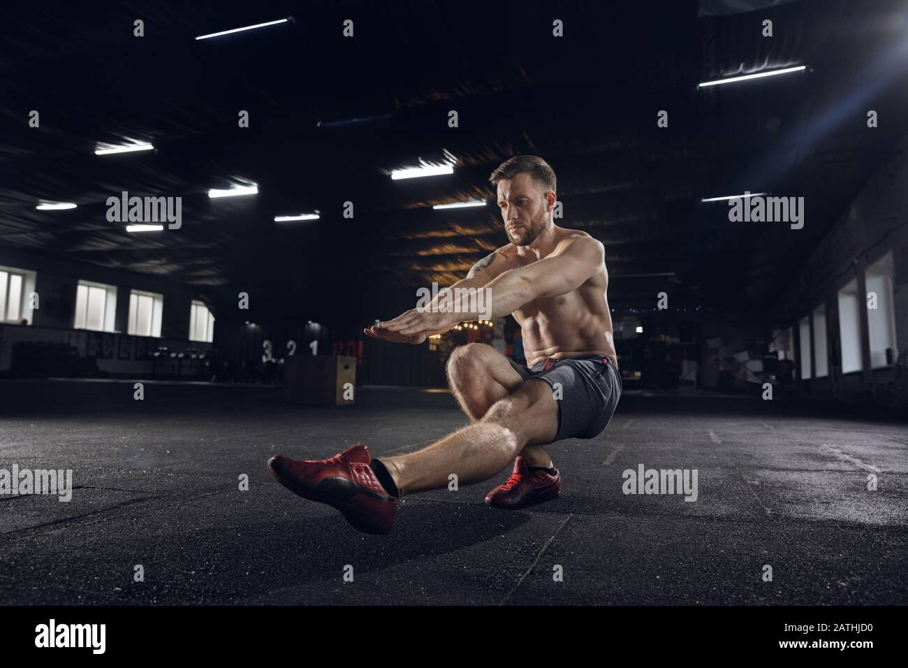 Young healthy man, athlete doing balance exercises, squats in gym ...