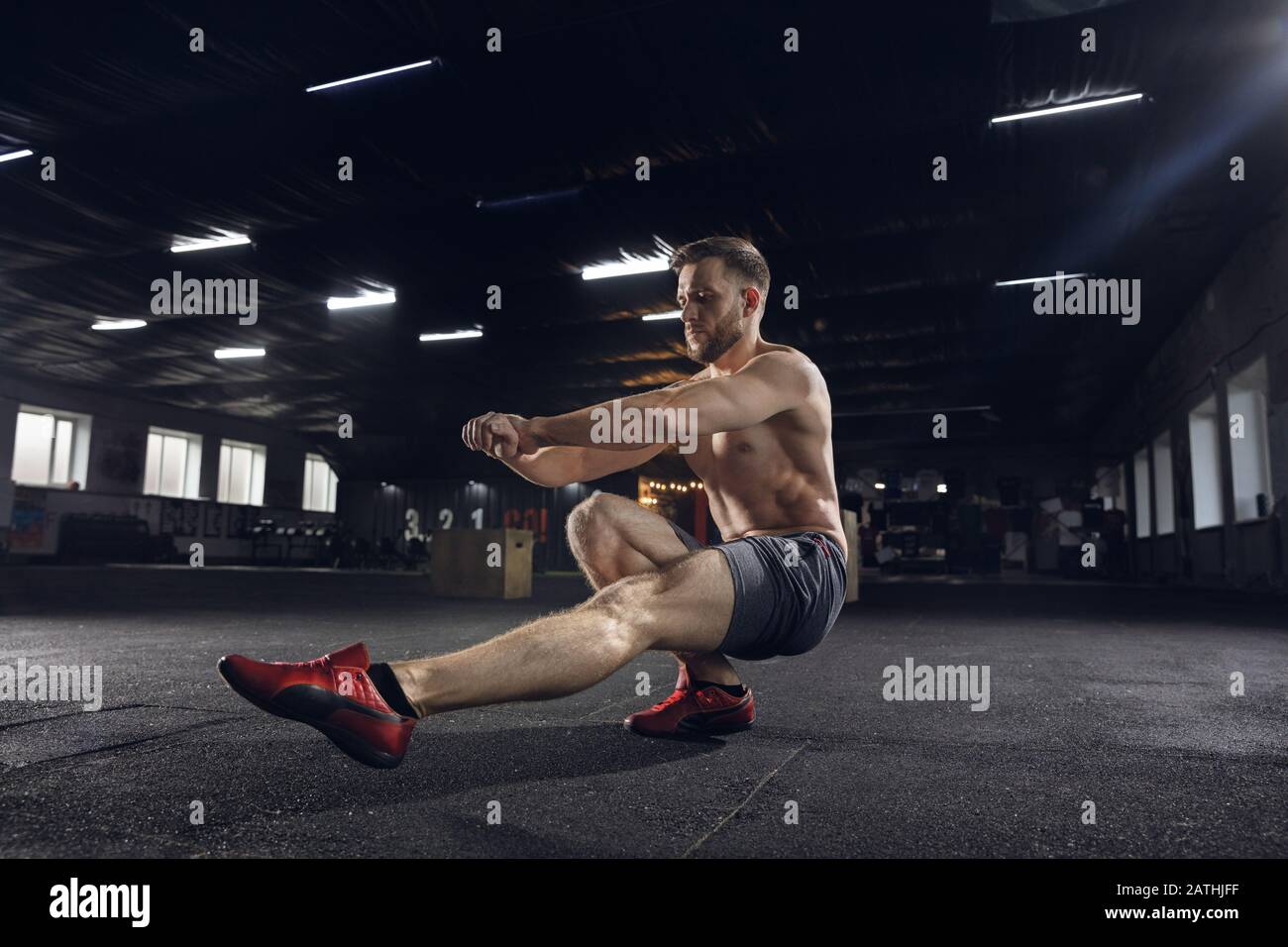 Young healthy man, athlete doing balance exercises, squats in gym ...