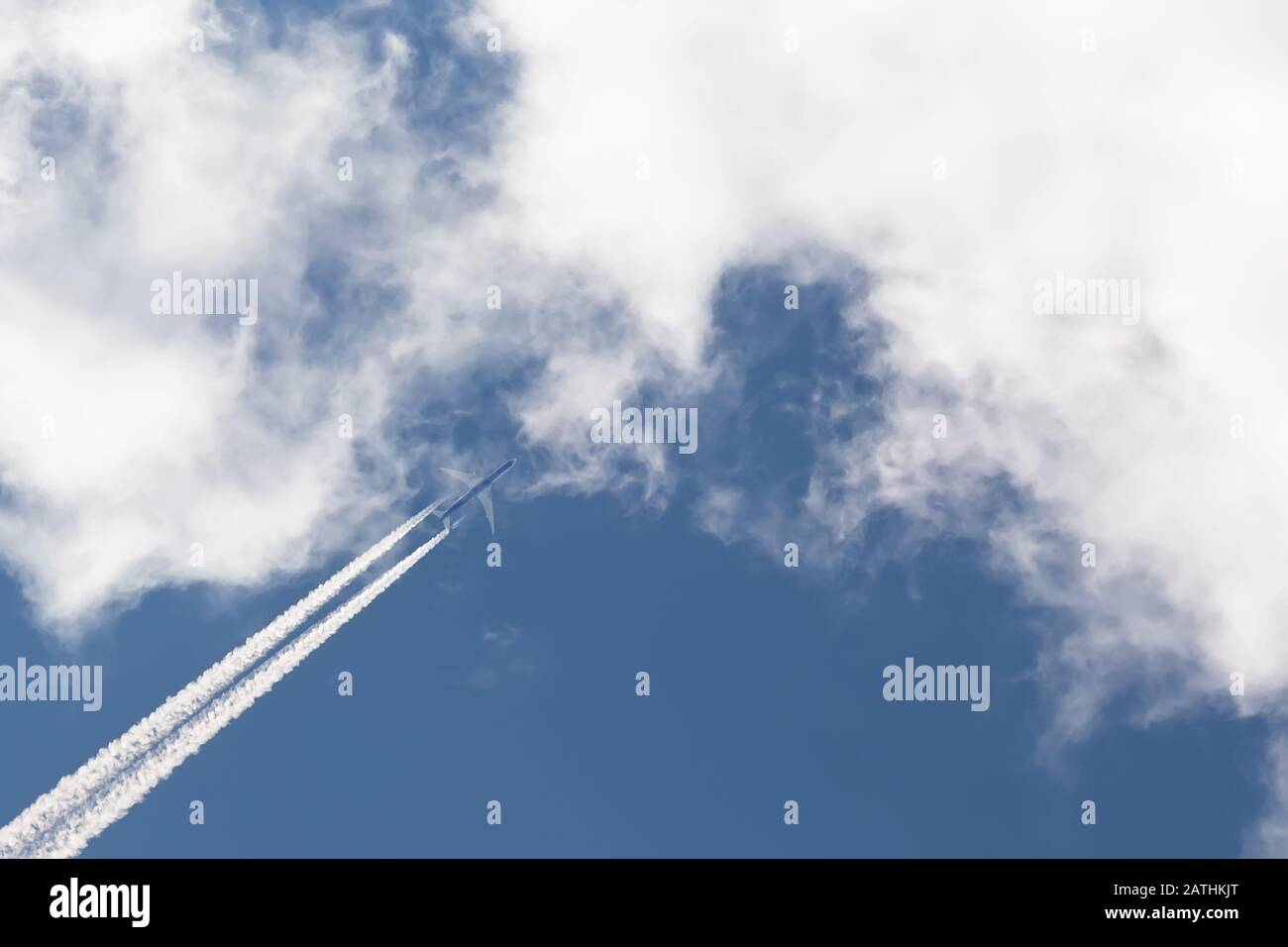 A twin-engine jet in the blue sky with clouds leaves an inversion mark ...