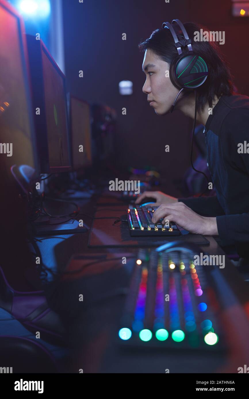 Vertical side view portrait of young Asian man using computer in cyber ...