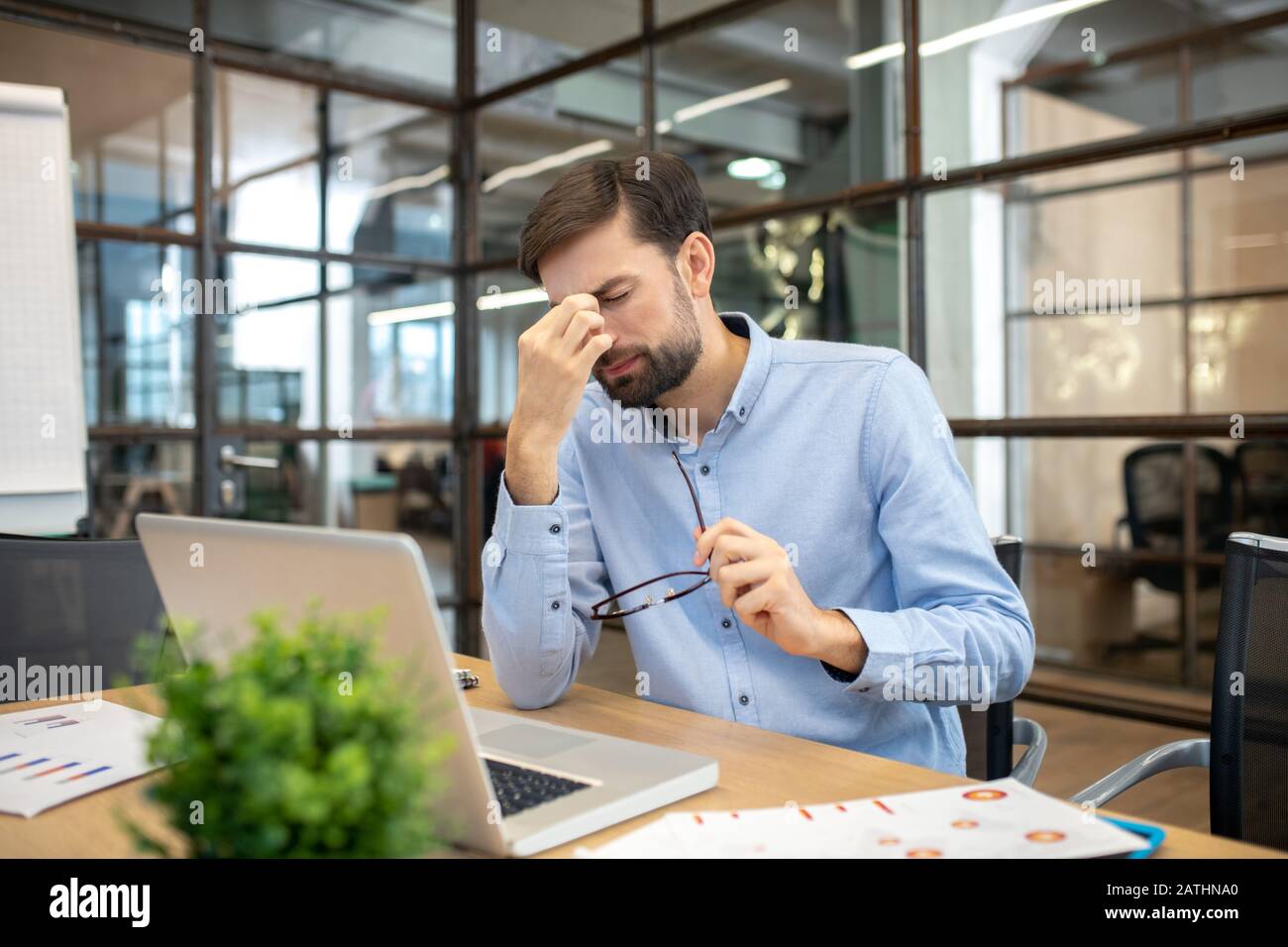 Bearded young man in a blue shirt feeling tired after work Stock Photo ...