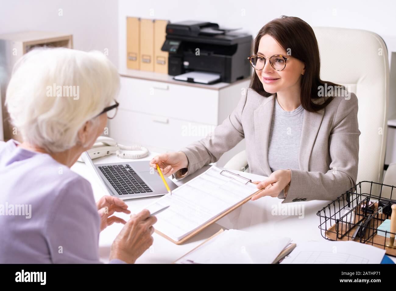 Smiling attractive young woman in glasses sitting at desk and pointing ...