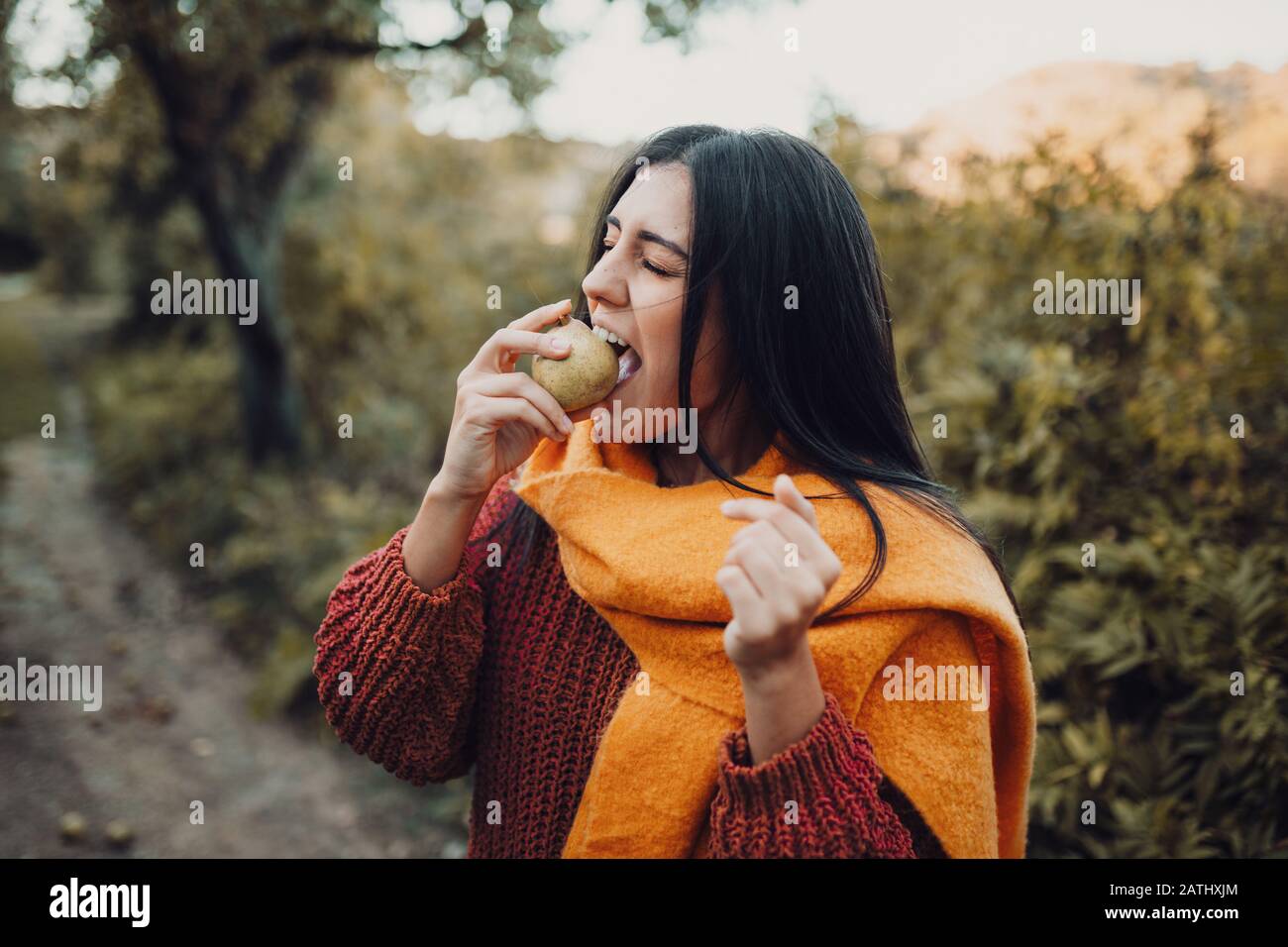 Young woman biting a pear in the field wearing a sweater Stock Photo ...