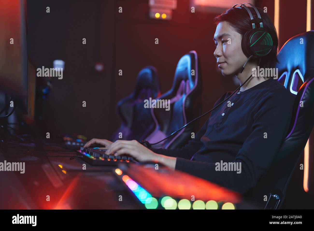 Side view portrait of smiling Asian man playing video games in pro ...