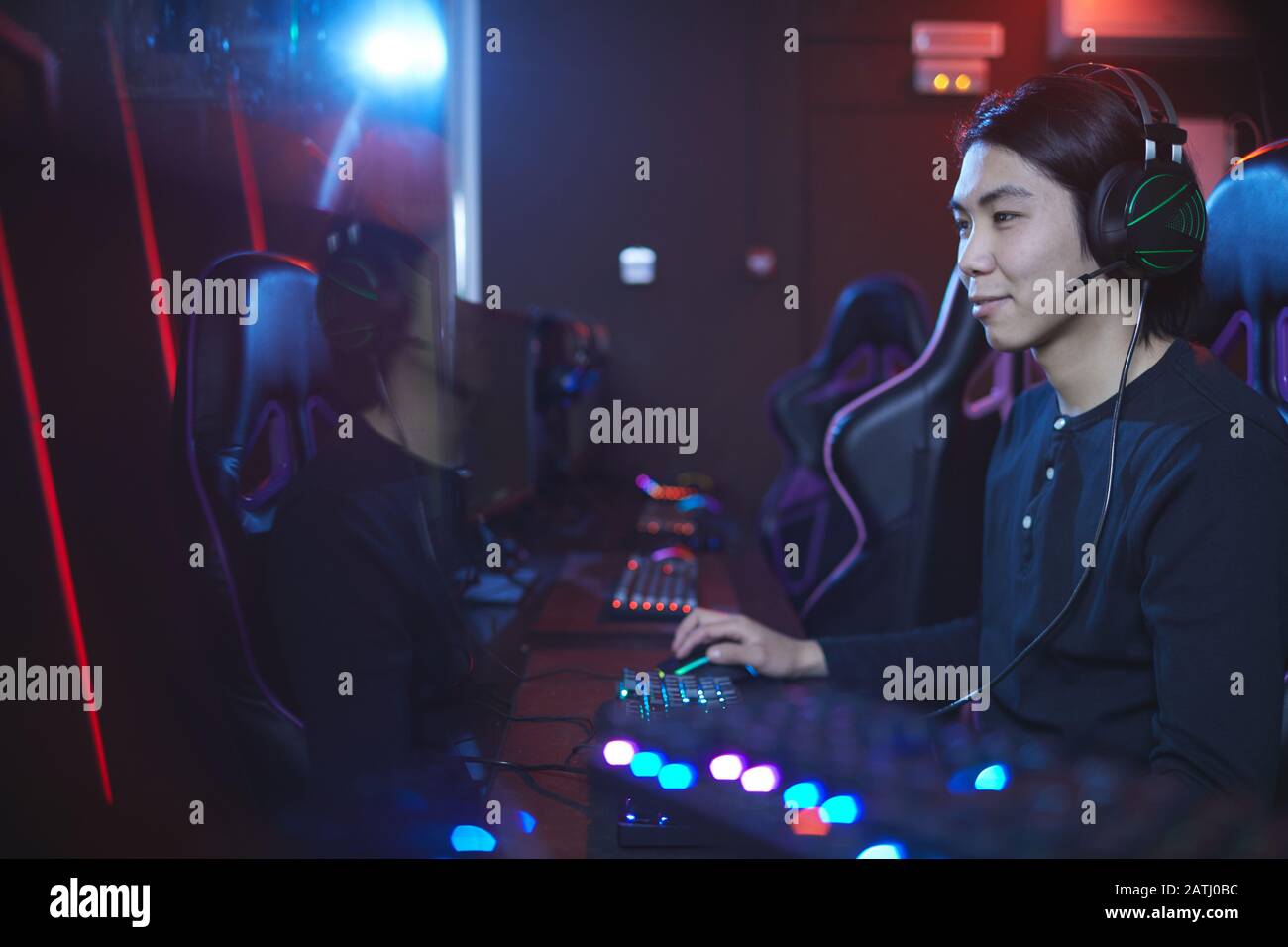 Side view portrait of smiling Asian pro-gamer enjoying videogames in ...