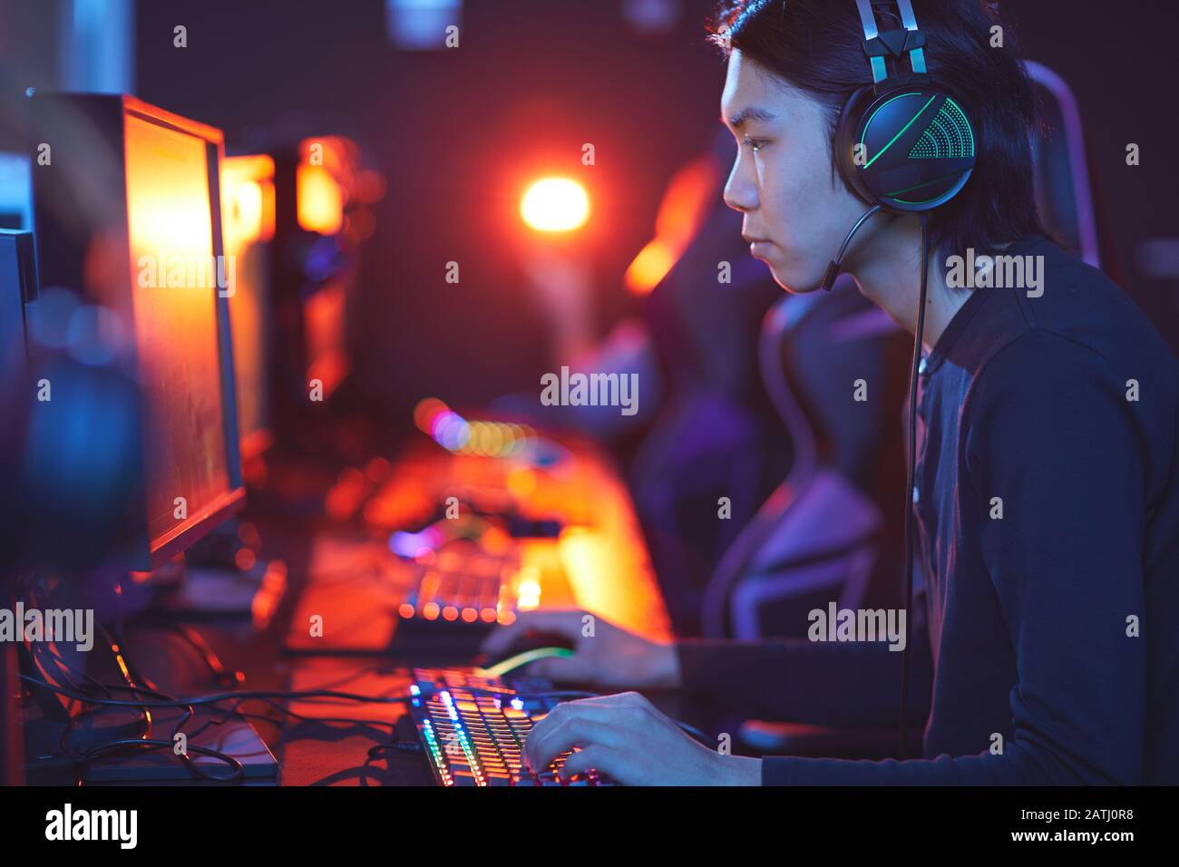 Side view portrait of young Asian man playing video game in dark room ...